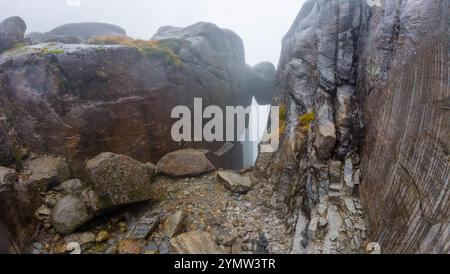 A large boulder wedged between two towering cliffs in a foggy landscape ...