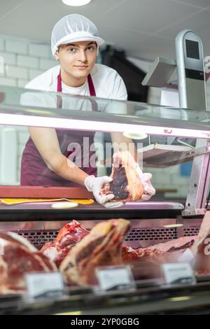 Positive young salesman demonstrating piece of meat in butcher shop ...