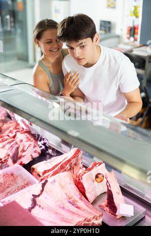 Spouse near butcher shop window inspects goods and choose piece of beef ...