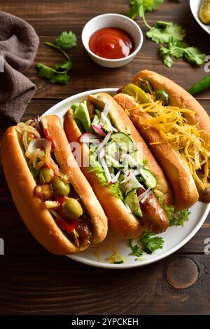 Hot dogs with different toppings on white plate on wooden background ...