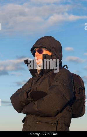 Mature man in a puffer jacket leaning on a metal railing outdoors ...