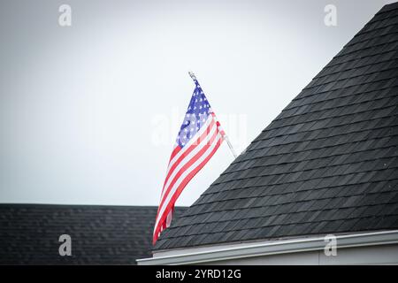 An American flag mounted on a rooftop with dark shingles, set against a ...