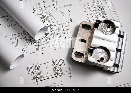 Metal part lying on engineering drawing with rolled blueprints ...