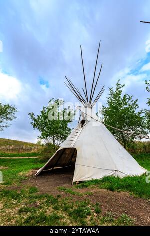 Teepee is standing in a grassy field. The teepee is white and has a ...