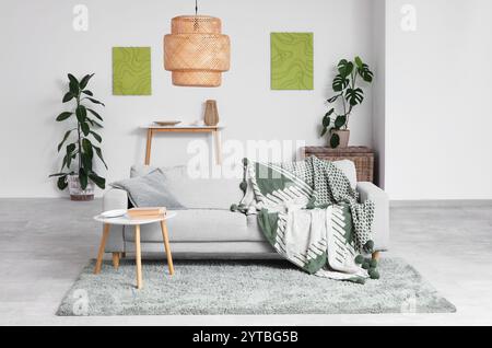 Comfortable sofa, coffee table, pictures and houseplants in interior of ...
