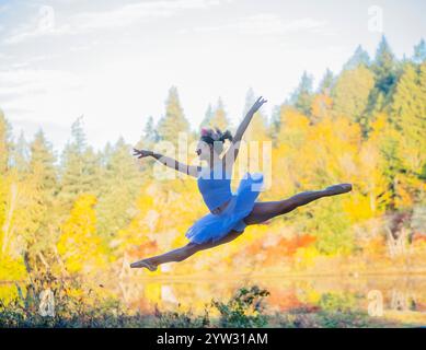 Ballet dancer performing a grand jetÈ in a park with beautiful autumn ...