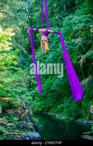 Aerial performer hanging upside down at sunset, silhouetted against a ...