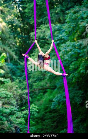 Female acrobat executing an aerial pose, hanging upside-down with red ...