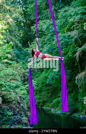 Aerial performer demonstrating a pose with purple silk fabric suspended from a bridge in a lush ...