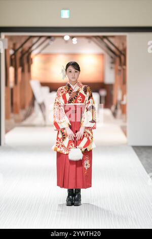 A Japanese woman in her 20s stands indoors wearing a red kimono (hakama ...