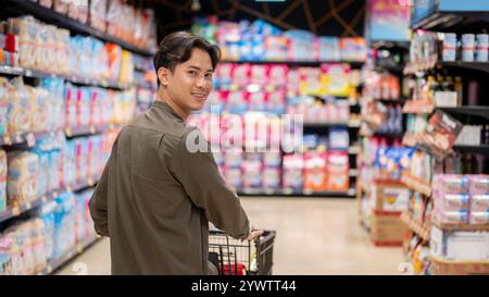 Man pushing shopping cart through supermarket aisle while buying ...