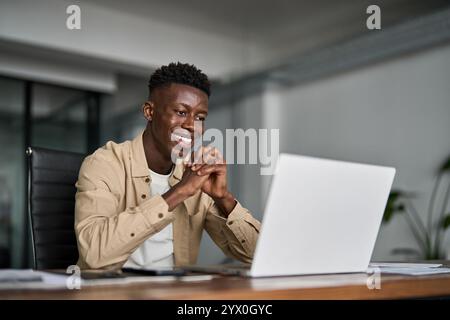 Happy young man working with laptop in armchair on light background ...