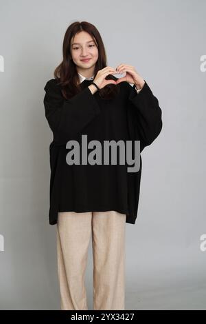 Joyful lady forms a heart with fingers, conveying feelings of affection ...