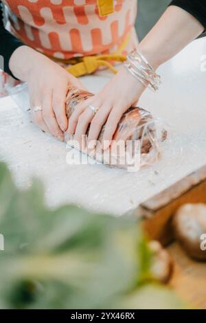 Woman wrapping fresh bread with baking paper on white wooden background ...