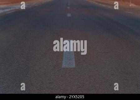 an asphalt road leading through a flat section of desert to the horizon ...