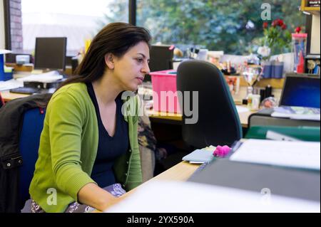 Female teacher working at her desk in staffroom open plan office space ...
