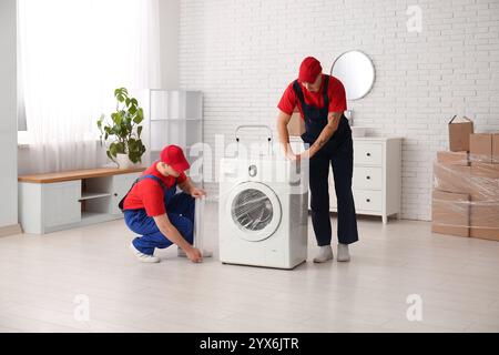 Male loaders wrapping washing machine with stretch film in room Stock ...