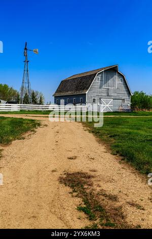 A windmill is on top of a red barn. The barn is surrounded by a fenced ...