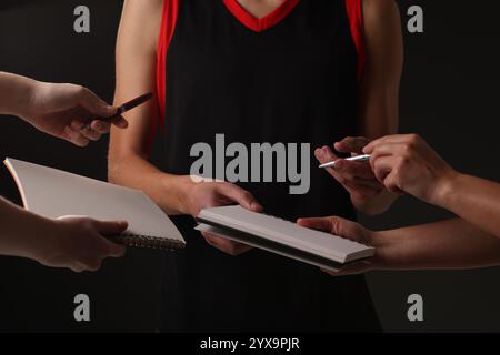 Sportsman signing autograph in notebooks on black background, closeup ...