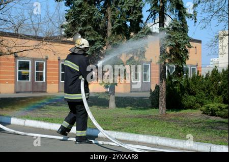 Fireman in protective costume watering plant territory with syringe ...