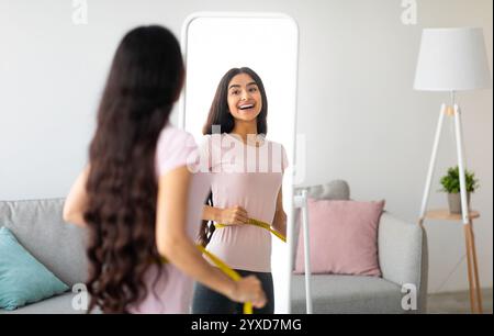 Young woman measuring a waist near the mirror Stock Photo - Alamy