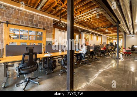 Tech entrepeneurs working at a long series of modular desks in tech ...