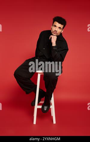 A man sits on a stool looking at his phone, with his feet up, in front ...