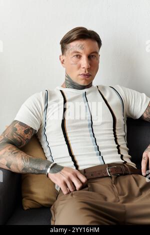 A young man with tattoos sits comfortably on a couch, engrossed in a ...