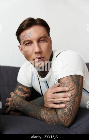 Stylish man with tattoos leans against a wall, soaking in sunlight in a ...