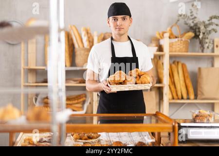 Smiling young bakery seller offering freshly baked pastries Stock Photo ...