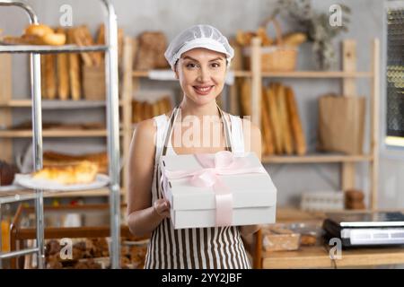 Young bakery seller offering gift-wrapped box with baked treats to ...