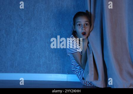 Scared girl hiding behind curtain at night. Space for text Stock Photo ...