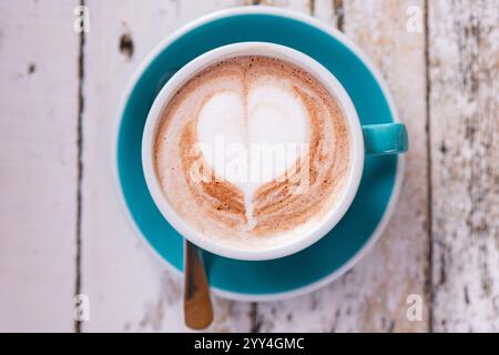 Close-up of creamy heart-shaped latte art in a turquoise cup on a ...