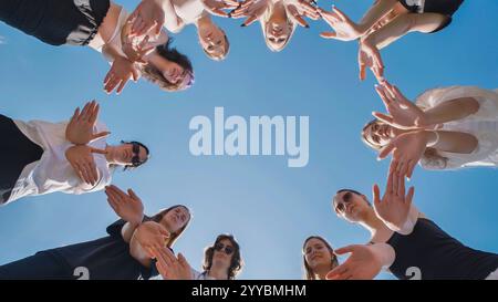 High school students joining hands in a circle under the clear blue sky ...
