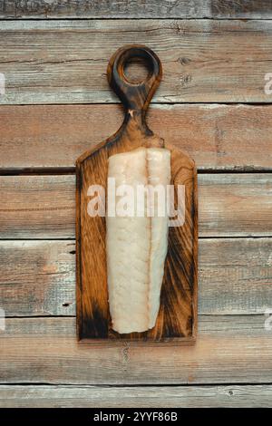 A raw fish fillet rests on a black slate board with peppercorns, salt ...