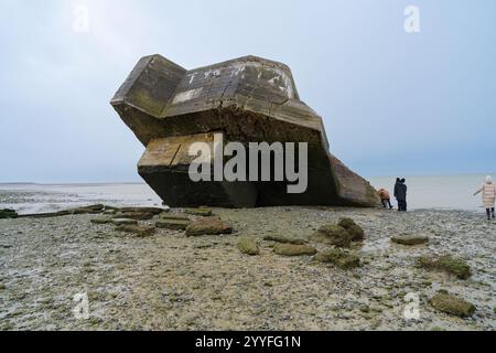 Concrete structure tilted on a sandy beach as visitors explore its ...