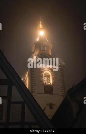 A church tower at night, shrouded in thick fog and illuminated by warm ...