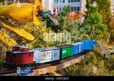 A model freight train winds through lush greenery on a railway bridge ...