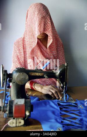 Indian woman stitching cloths by machine and using mobile Stock Photo ...