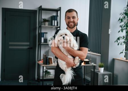 Man is smiling. Groomer is with Maltese dog indoors. Man is in the ...