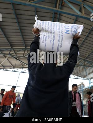 Workers move sacs of flour as Palestinians queue to receive food aid ...