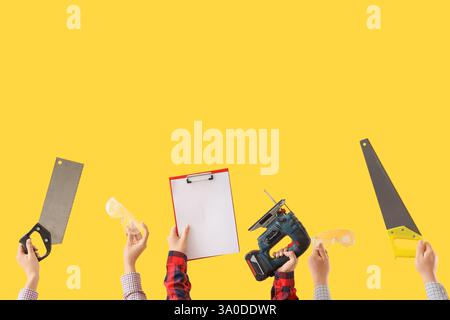 Hands holding construction tools and clipboard on yellow background ...