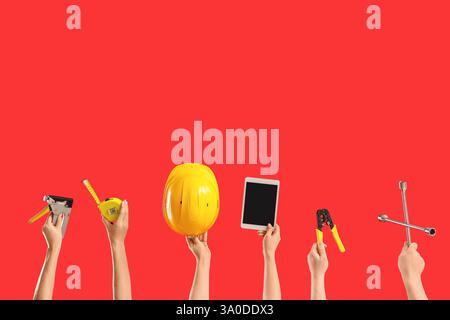 Hands holding construction tools and tablet computer on red background ...