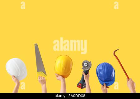 Hands holding construction tools, hardhats and drawings on yellow ...