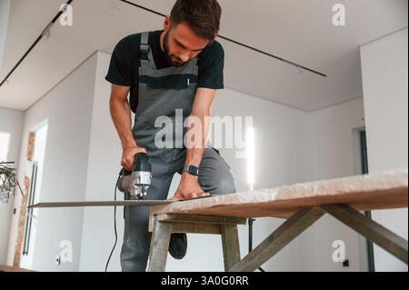 Using jigsaw to cut pieces. Man is installing new laminate wooden floor ...