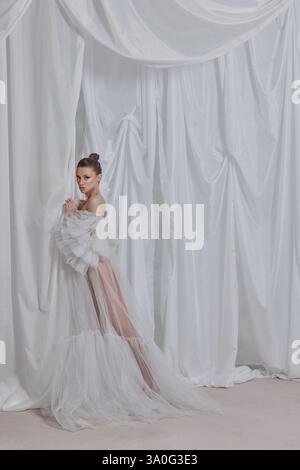 A model gracefully poses in a draped white fabric in a dark studio ...
