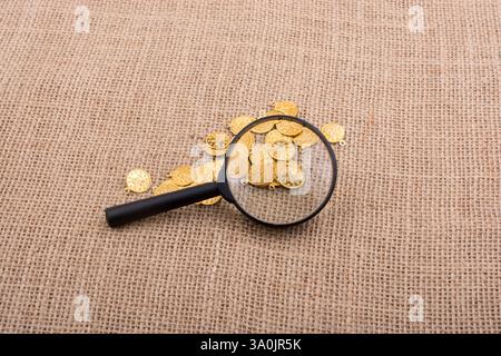 Plenty of fake gold coins behind magnifying glass Stock Photo - Alamy