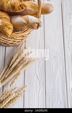 croissants and baguettes in wicker basket ears of wheat on white wooden ...
