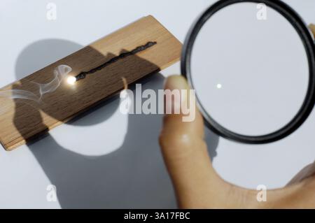 Magnifying glass focused on piece of wood starting fire Stock Photo - Alamy