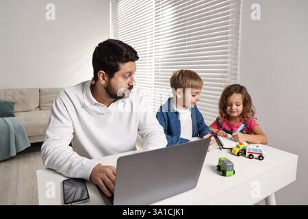 Naughty children and their overwhelmed father at table with laptop ...